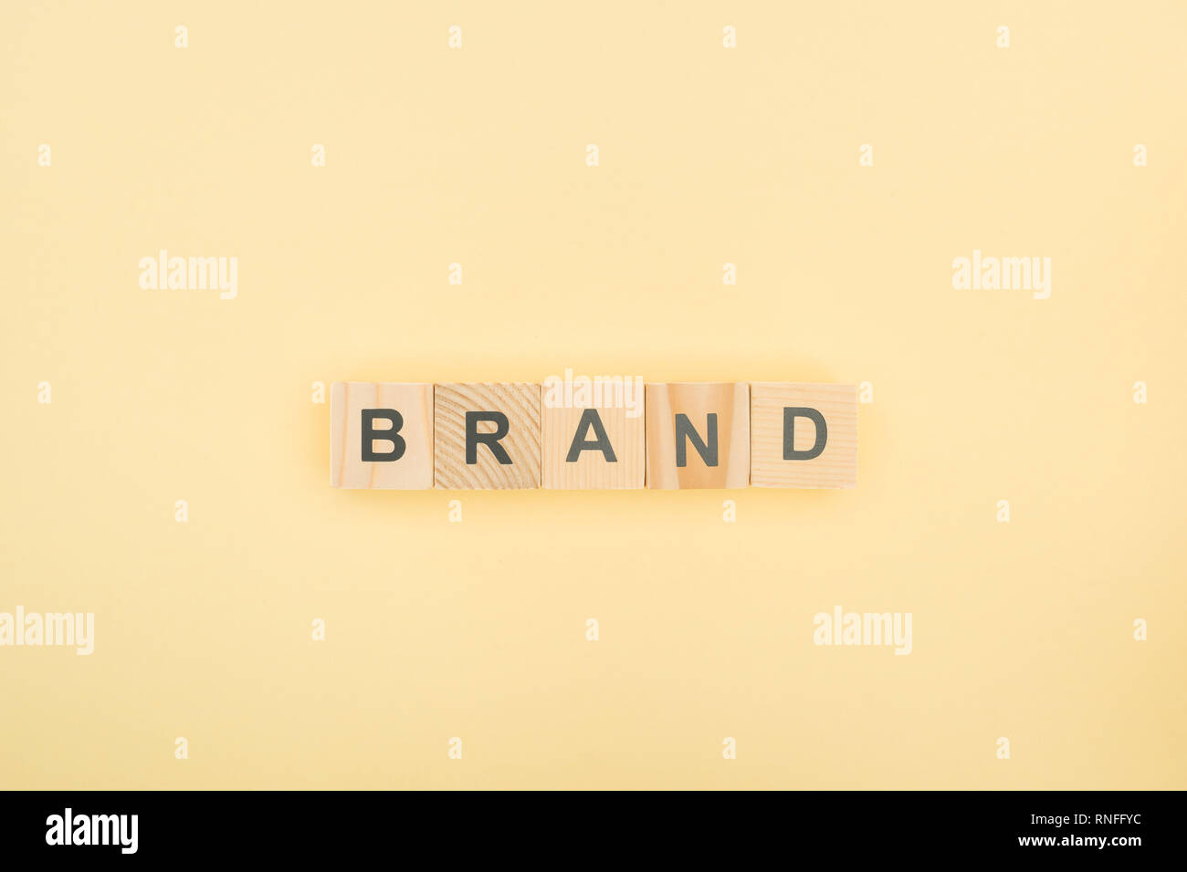 top view of brand lettering made of wooden cubes on yellow background ...