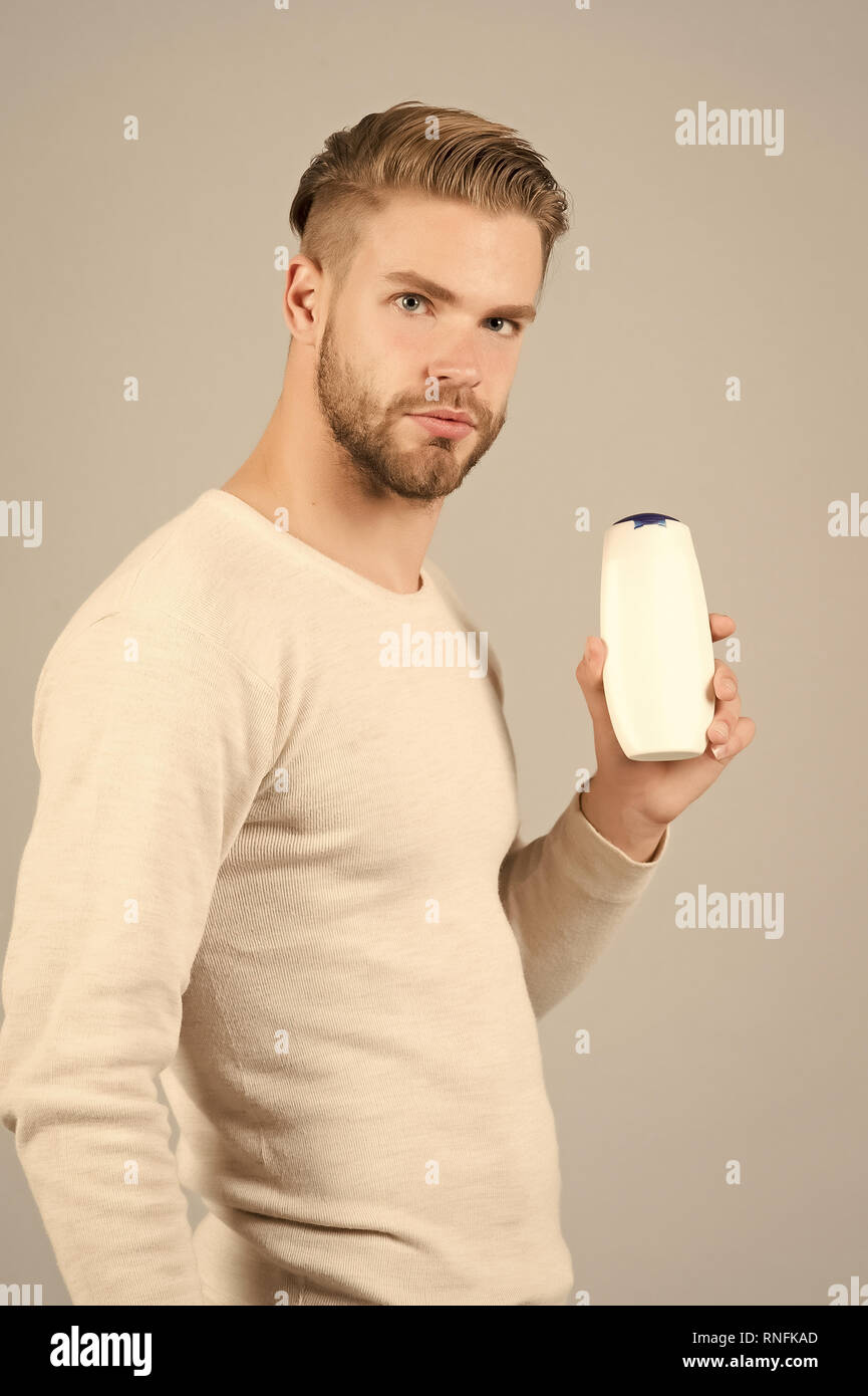 Man confident face holds shampoo bottle, grey background. Guy with ...