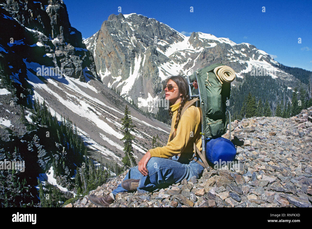 A female backpacker rests on a scree slope as she negotiates a rugged ...