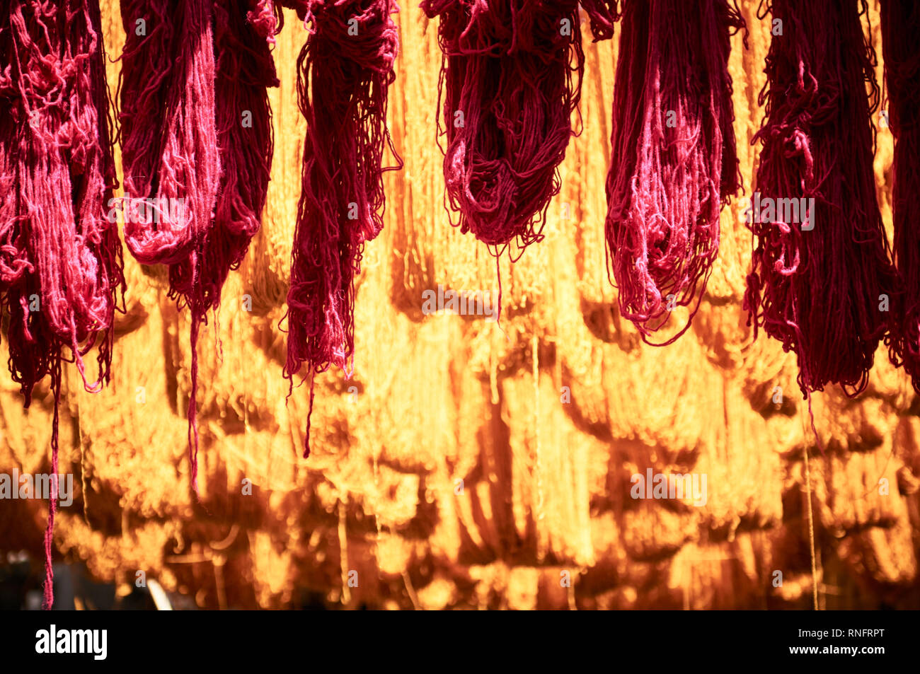 Bundles of wool string hang from bamboo poles overhead to dry in the ...