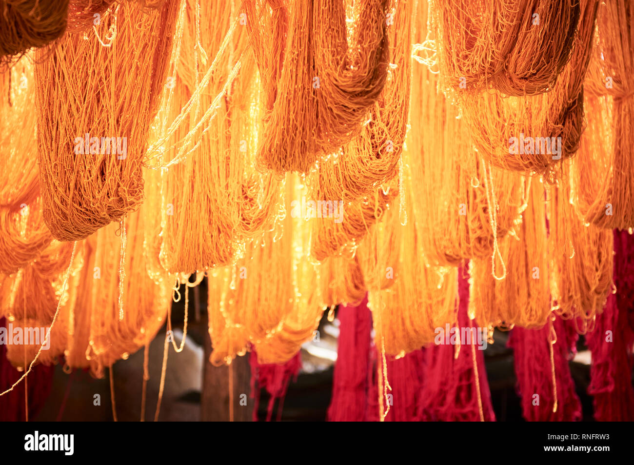 Bundles of wool string hang from bamboo poles overhead to dry in the ...