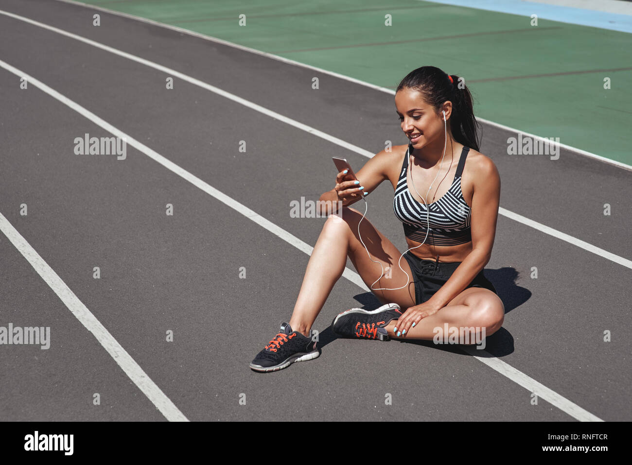 Young woman wearing black sportswear sitting on racetrack and holding ...