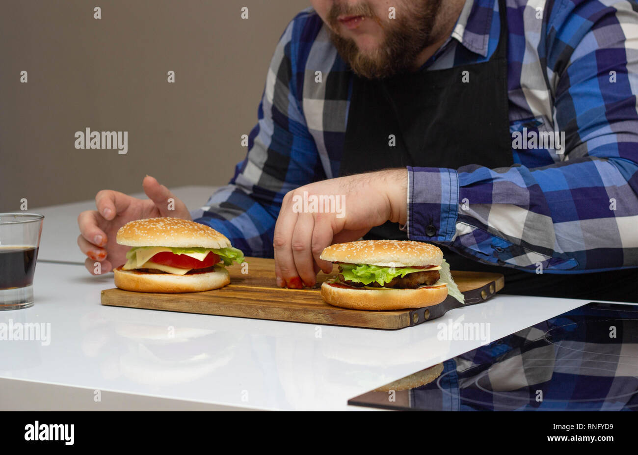 Fat man with a beard in a plaid shirt eats fast food cheeseburger and ...