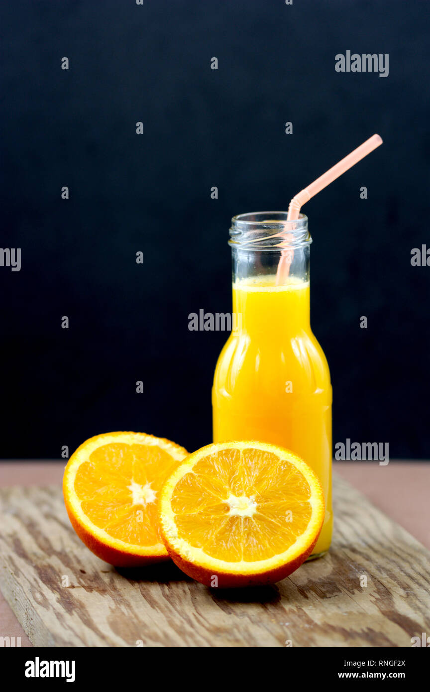 Still life of orange juice in a small bottle and an orange split in two ...