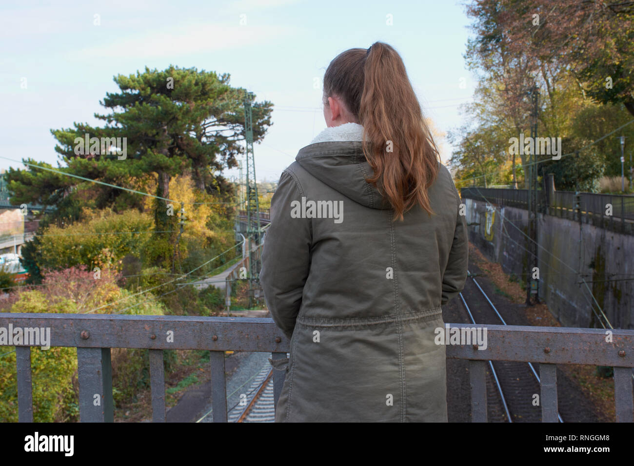 teenager girl is standing alone on a bridge and looks to the railroad ...