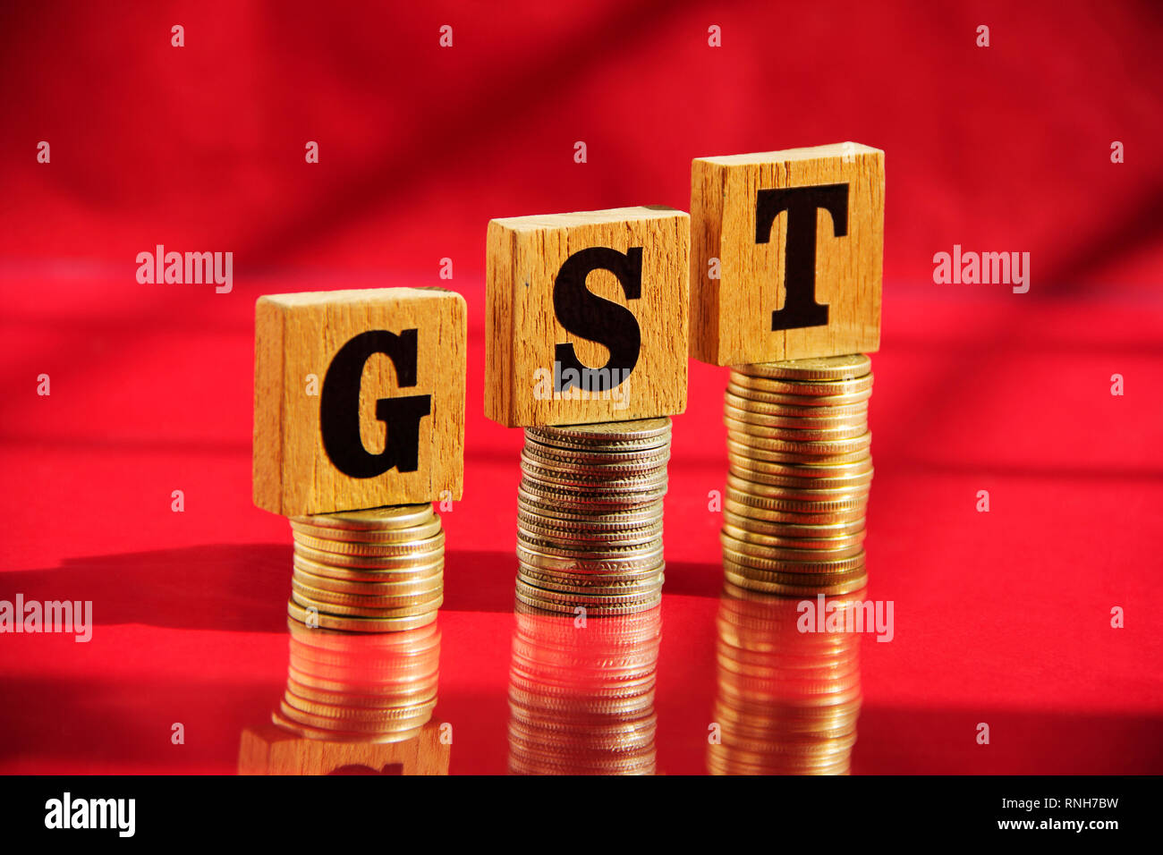 Wooden letters GST and money coin stack on red table background ... Wooden letters GST and money coin stack on red table background ...