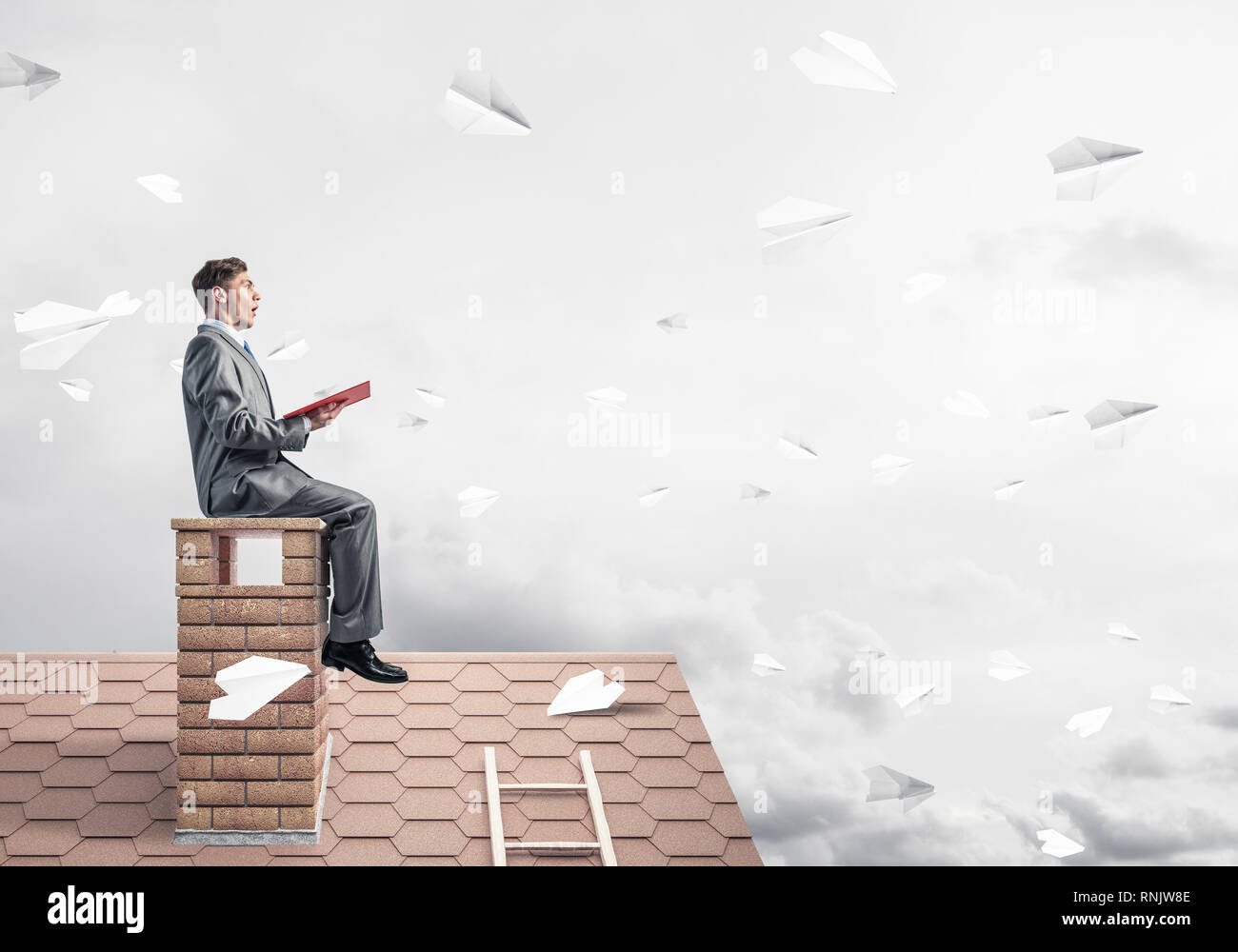 Man on brick roof reading book and paper planes flying in air Stock ...
