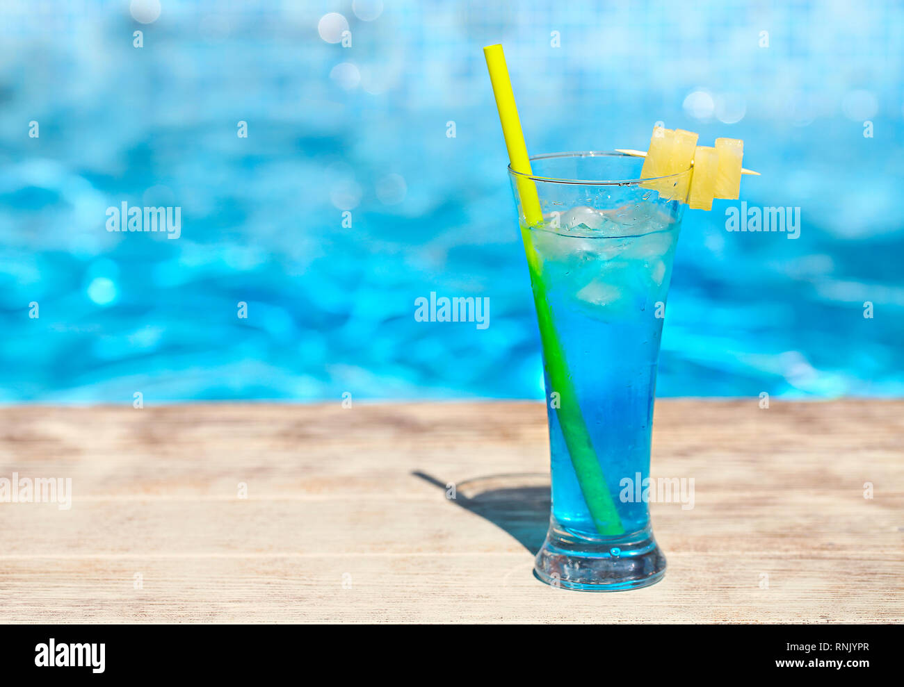 Glass with a bright blue lagoon cocktail on the table by the pool ...