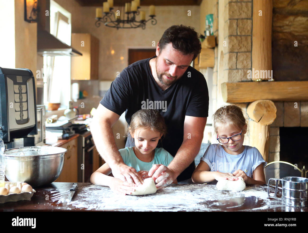 Father and his two little helpers. Children cooking homemade bread with ...
