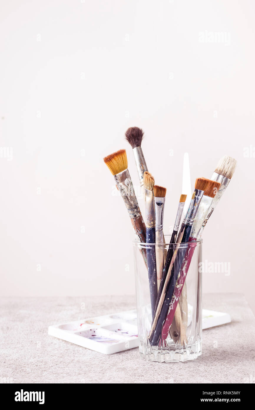 Glass with artistic brushes and palette on gray table Stock Photo - Alamy