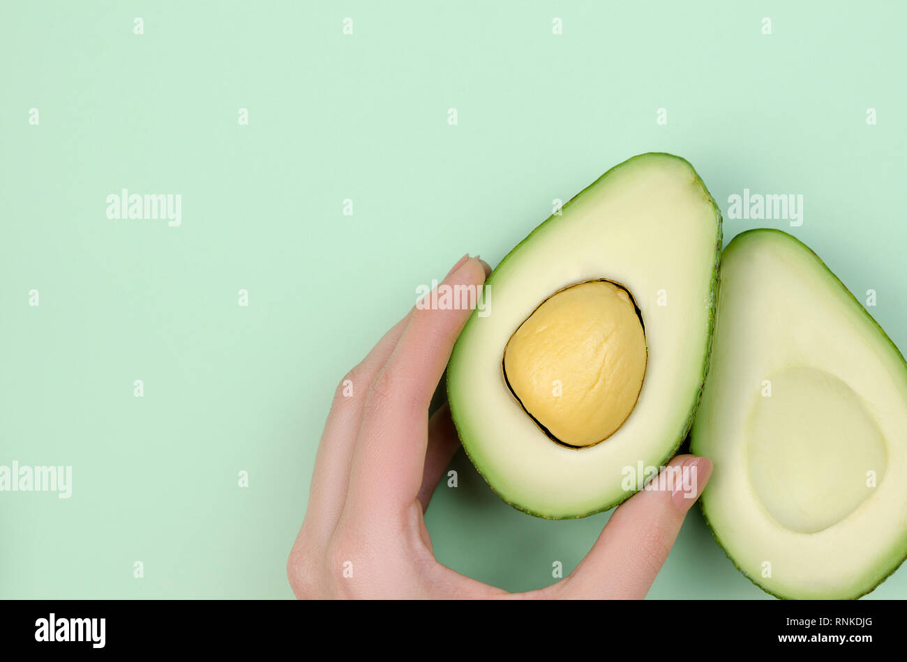 Avocado in female hand on light green background Stock Photo - Alamy
