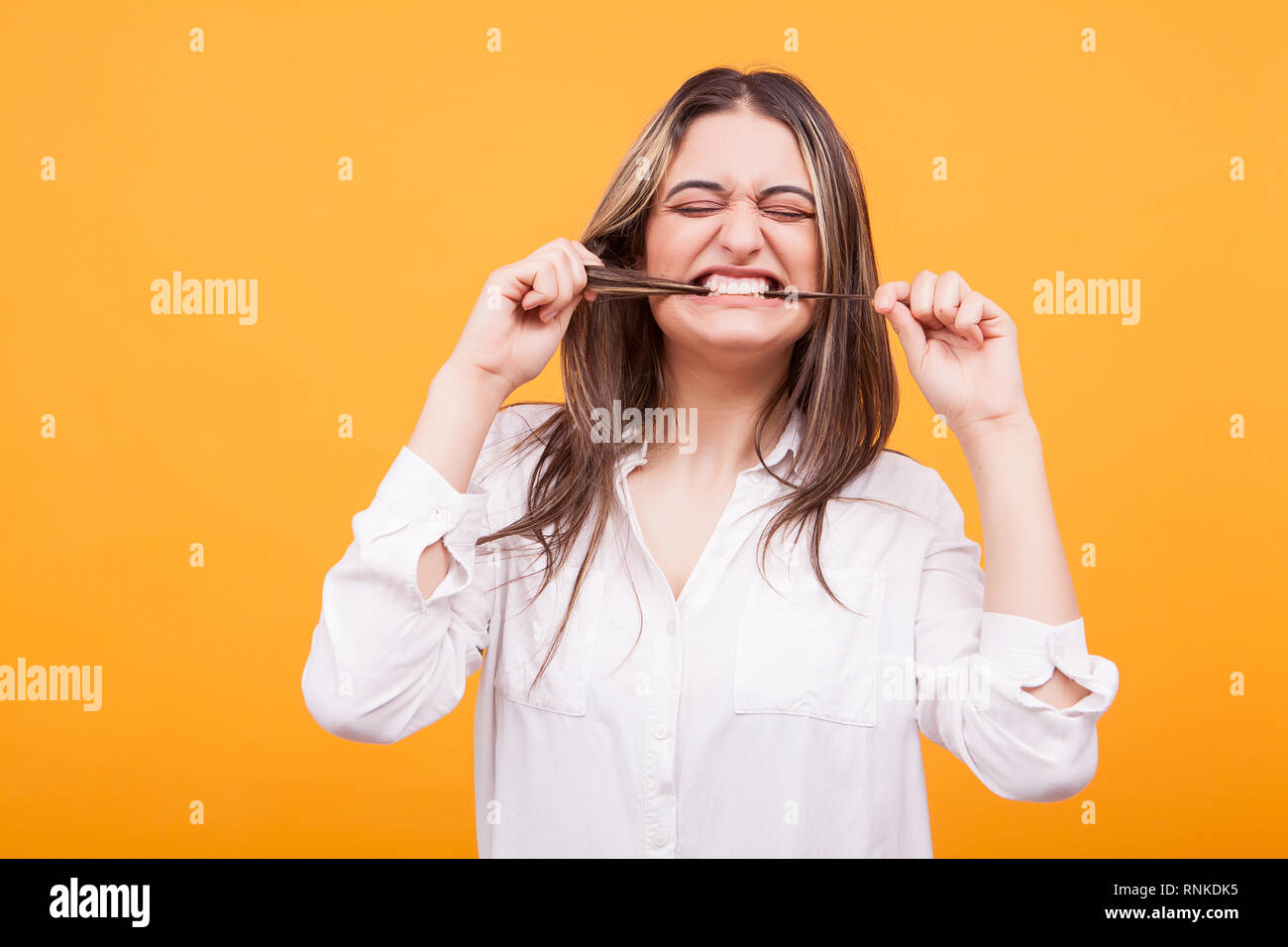 Silly young girl in white shirt biting her hair over yellow background ...