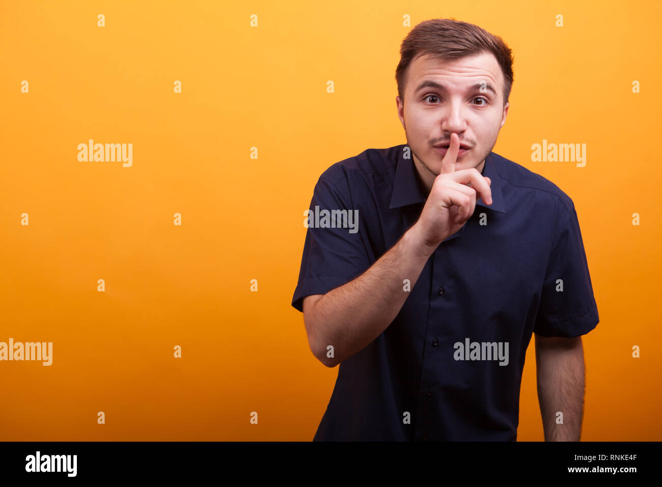 Close up portrait of young man in blue shirt showing shh sign over his ...
