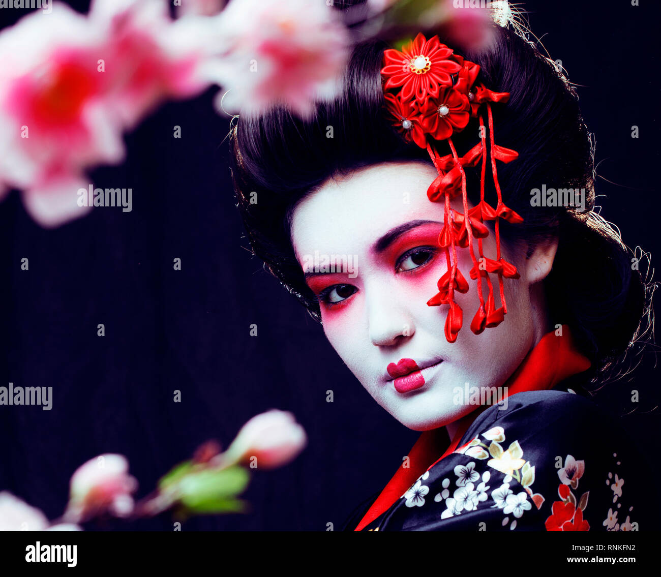young pretty real geisha in kimono with sakura and decoration on black ...