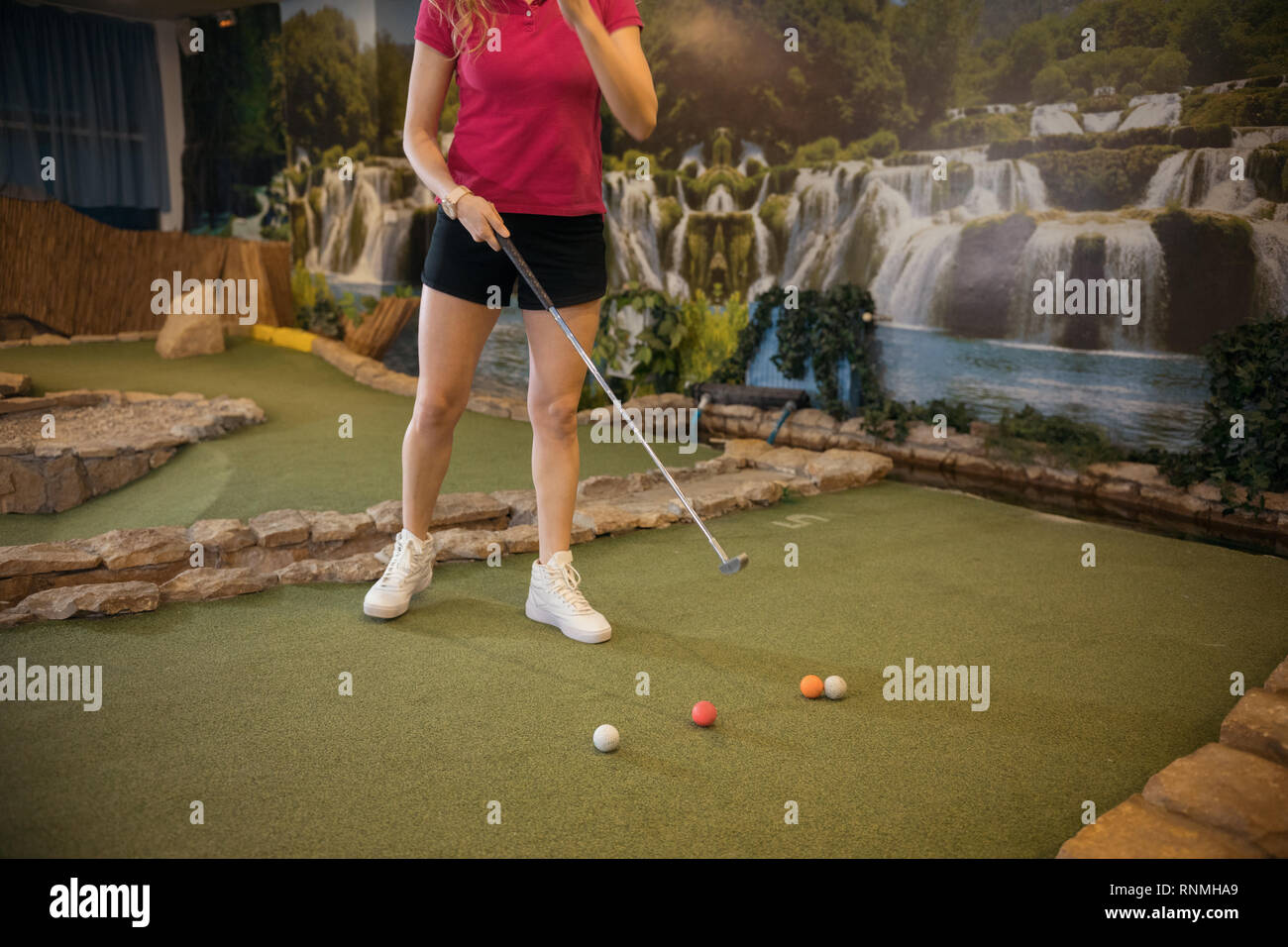 A young woman playing mini golf indoors. Legs in the frame Stock Photo ...