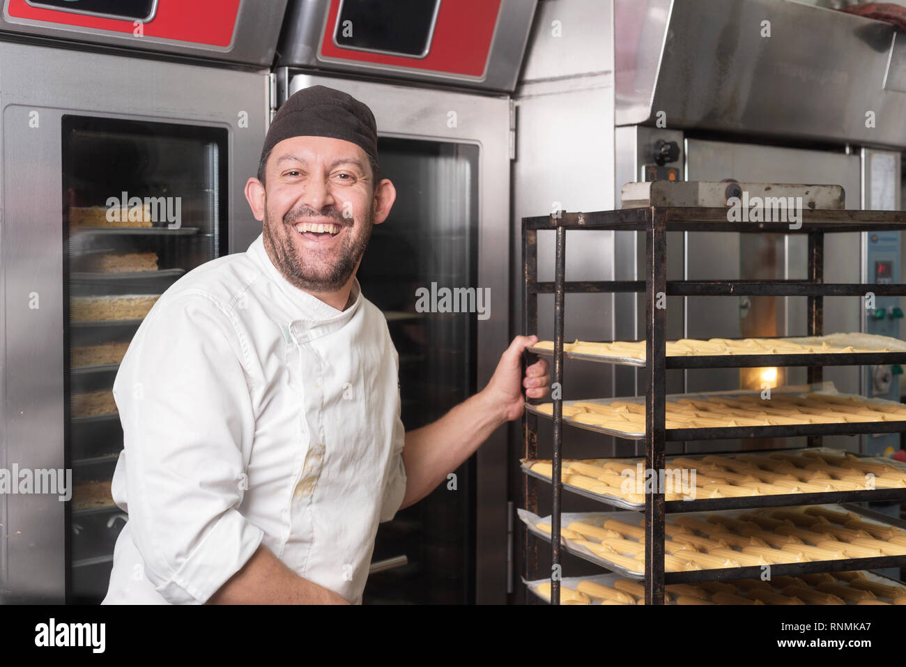 Smiling Baker putting a rack of pastries into the oven in bakery or ...