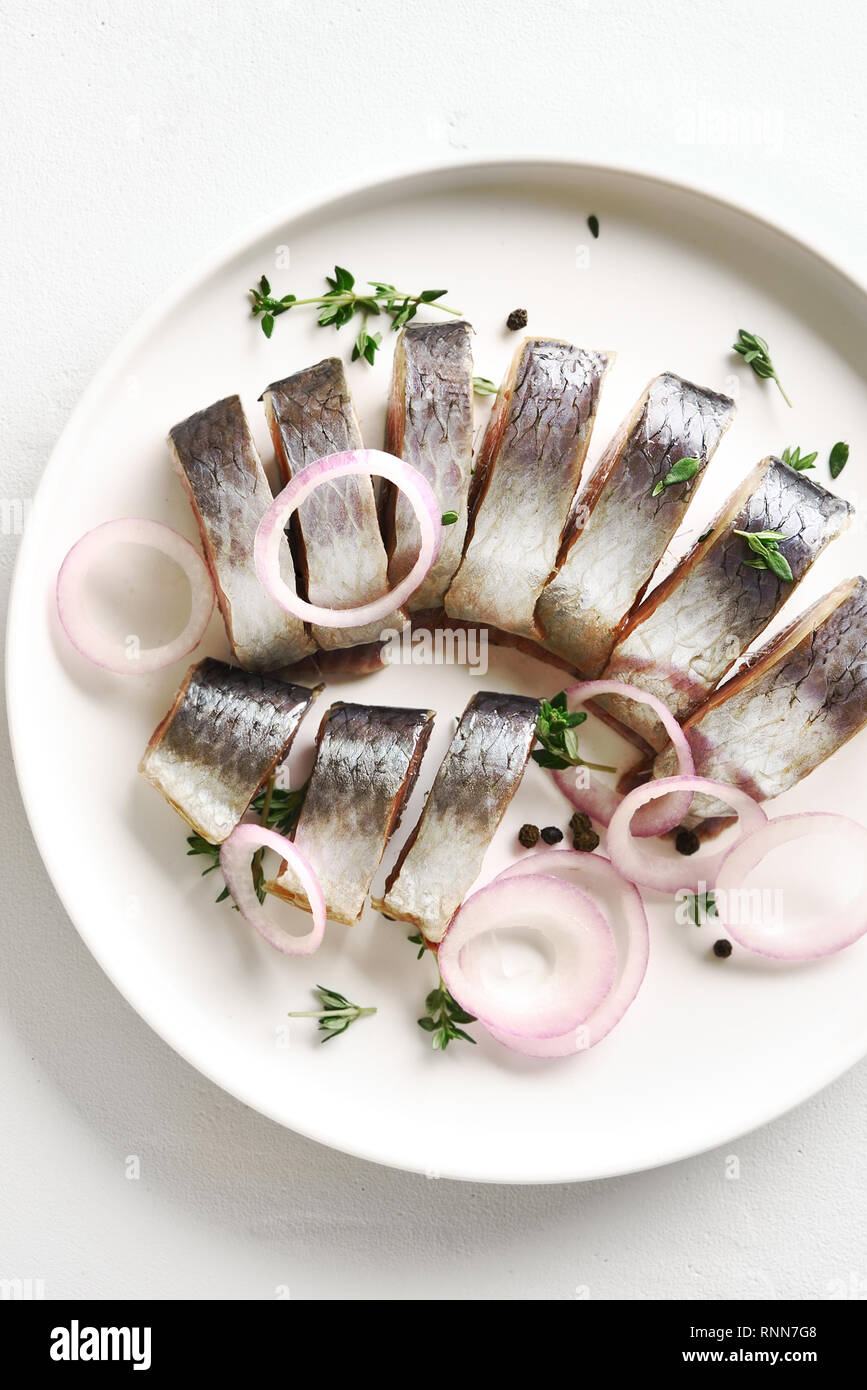 Close up of salted herring fillet with spice, herbs and onion on plate ...