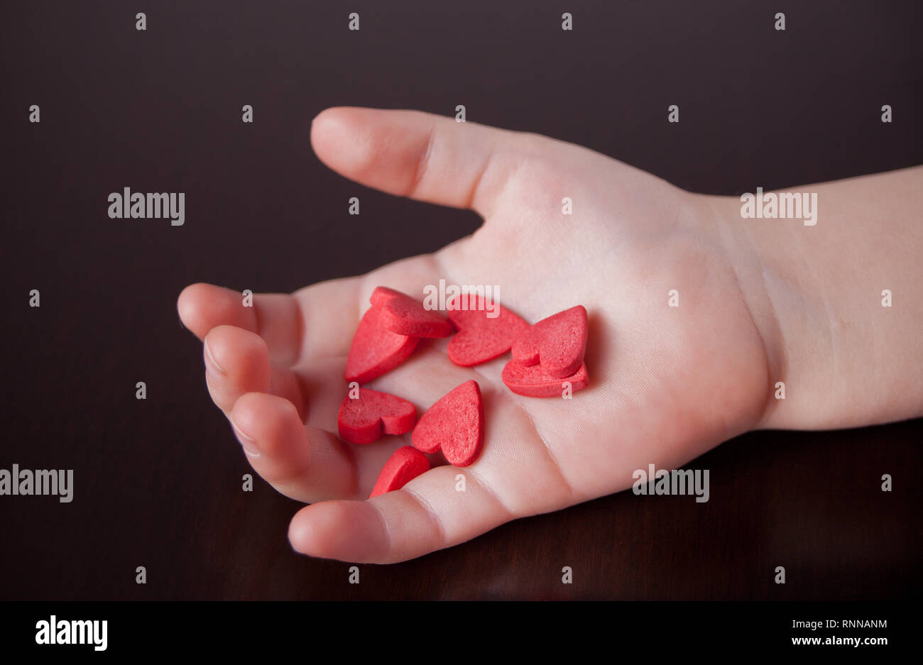 Child's hand holding red hearts on black background Stock Photo - Alamy