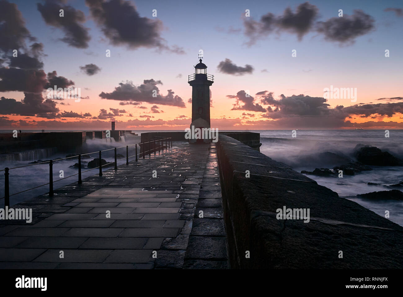 Lighthouse on the end of the jetty at sunsethour Stock Photo - Alamy