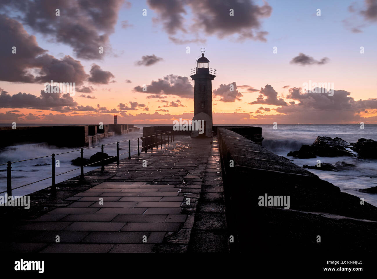 Lighthouse on the end of the jetty at sunsethour Stock Photo - Alamy
