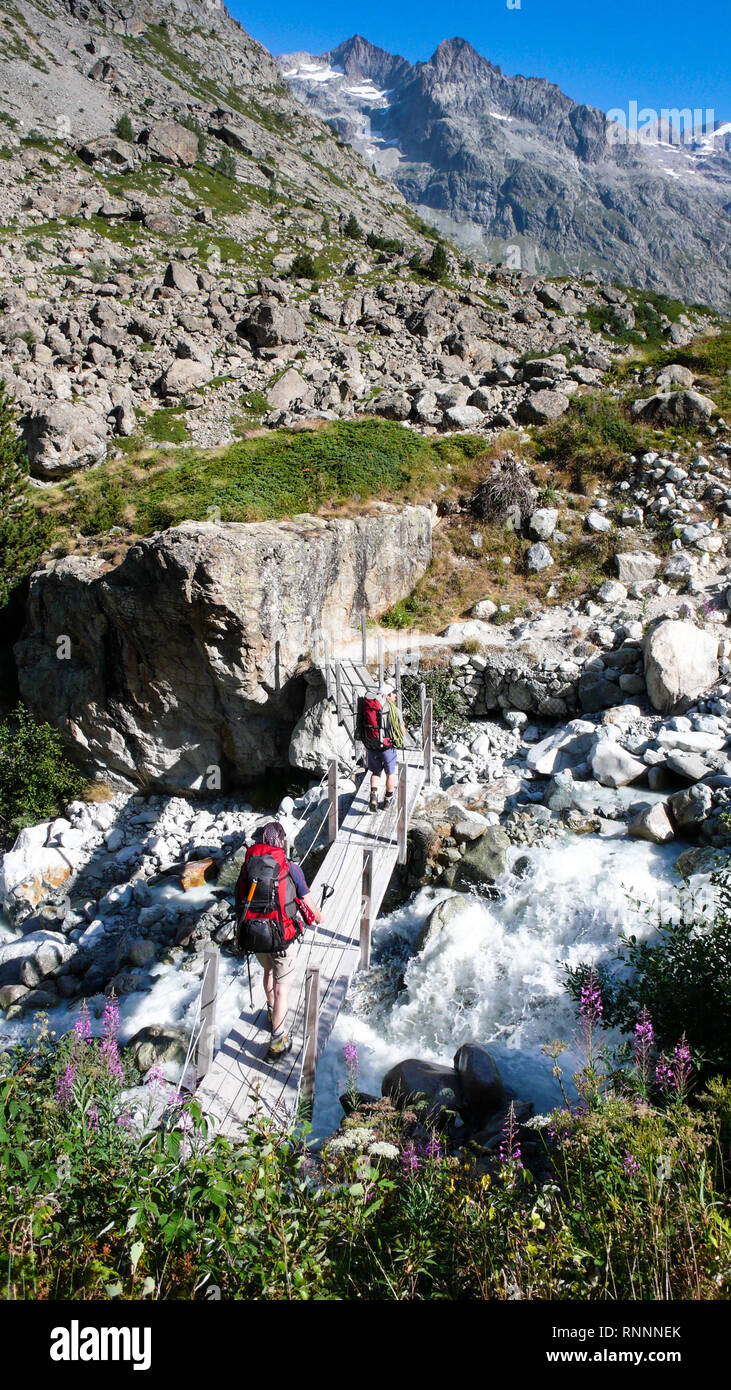 two hikers and mountain climbers cross a small stream over an old ...