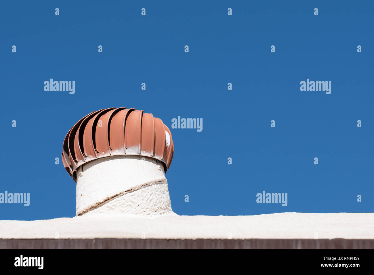 red spinning roof ventilation on a white roof with bright blue sky ...