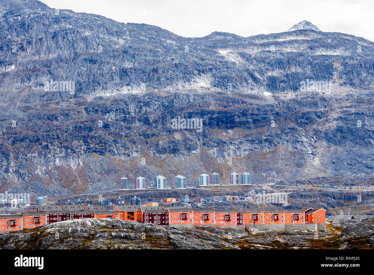 Rows of colorful modern Inuit houses among mossy stones with grey steep ...