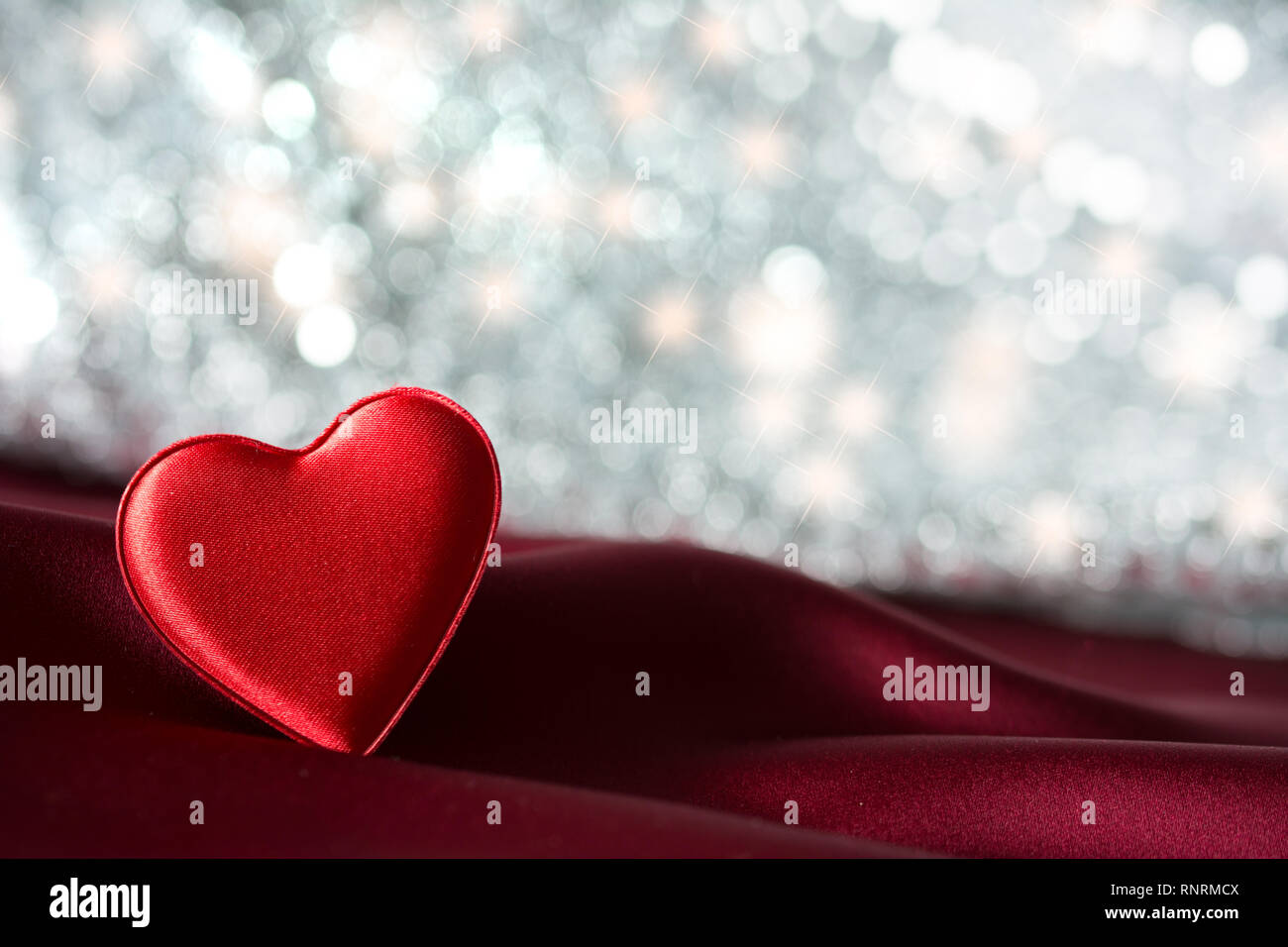 Single red heart on dark red satin - silver glossy background with ...