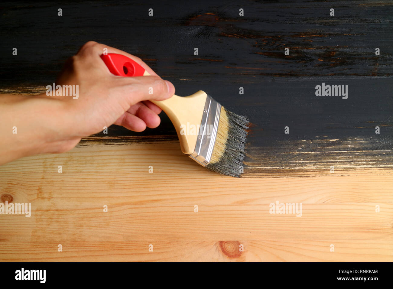 Man's hand holding brush painting wood plank with dark grey paint Stock ...