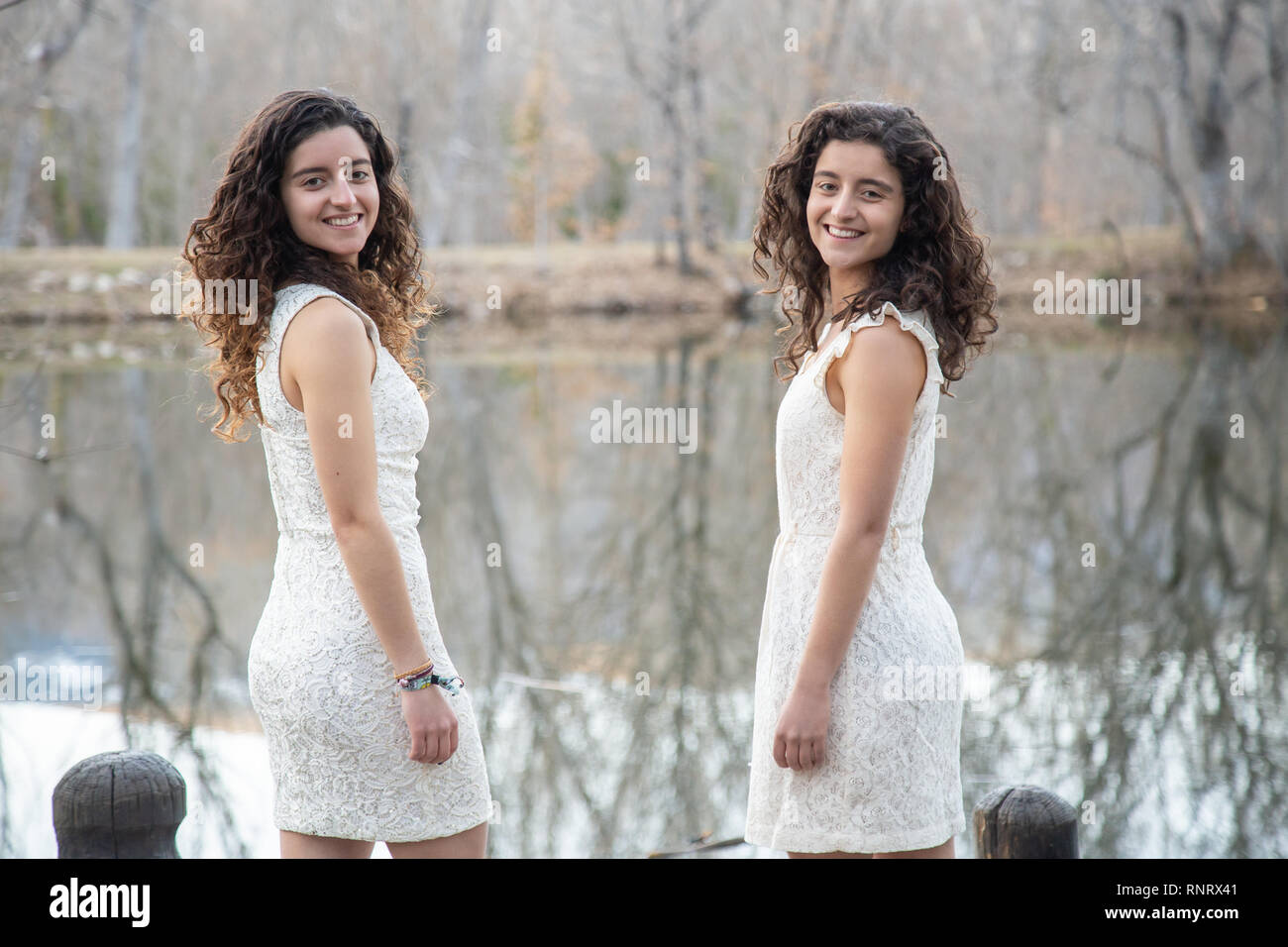 Side view of cheerful twin sisters standing at calm lake smiling and ...