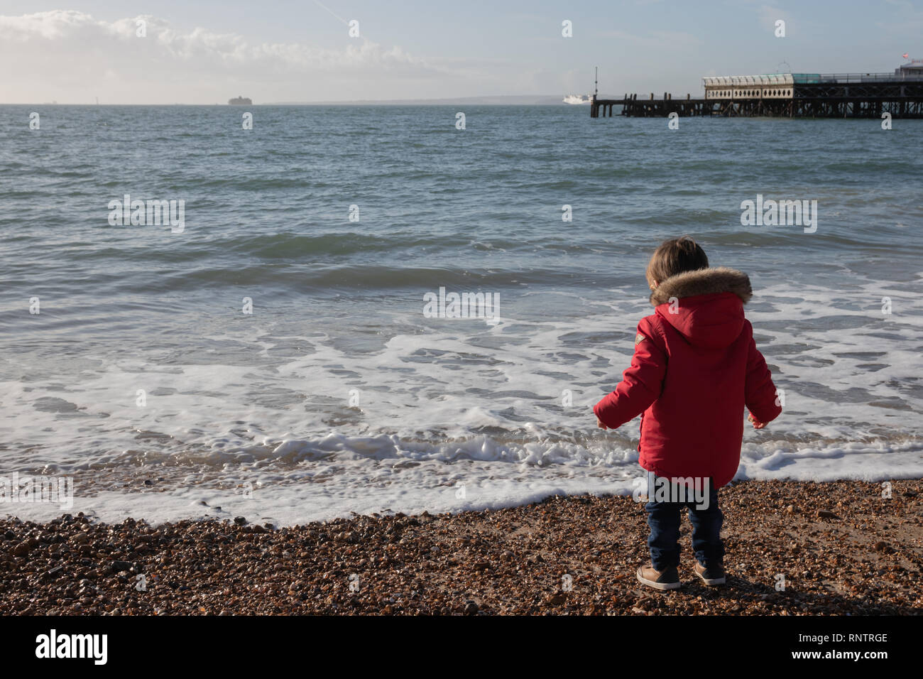 Toddler playing on pebble beach in a winter coat Stock Photo - Alamy