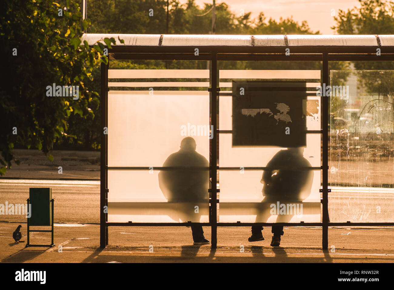 two men sit at a stop lit with the bright morning sun. They expect the ...
