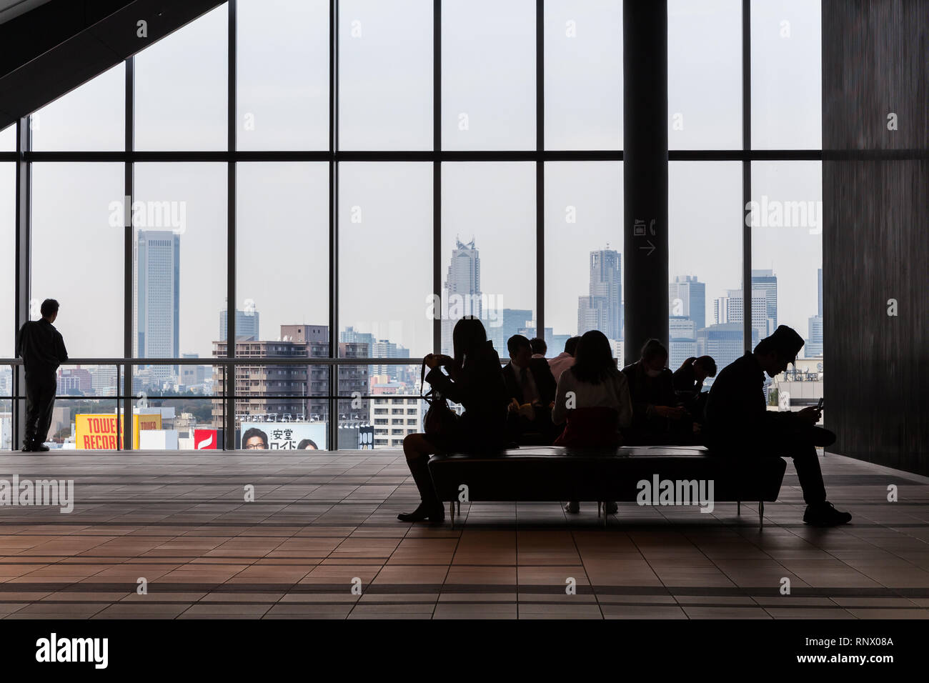 Japanese people sit at a bench and look out the windows at a view of ...