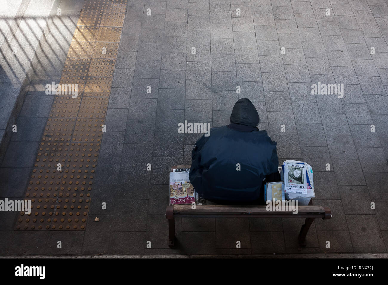 A homeless man reading as he rests on a bench in a small park in Tokyo ...
