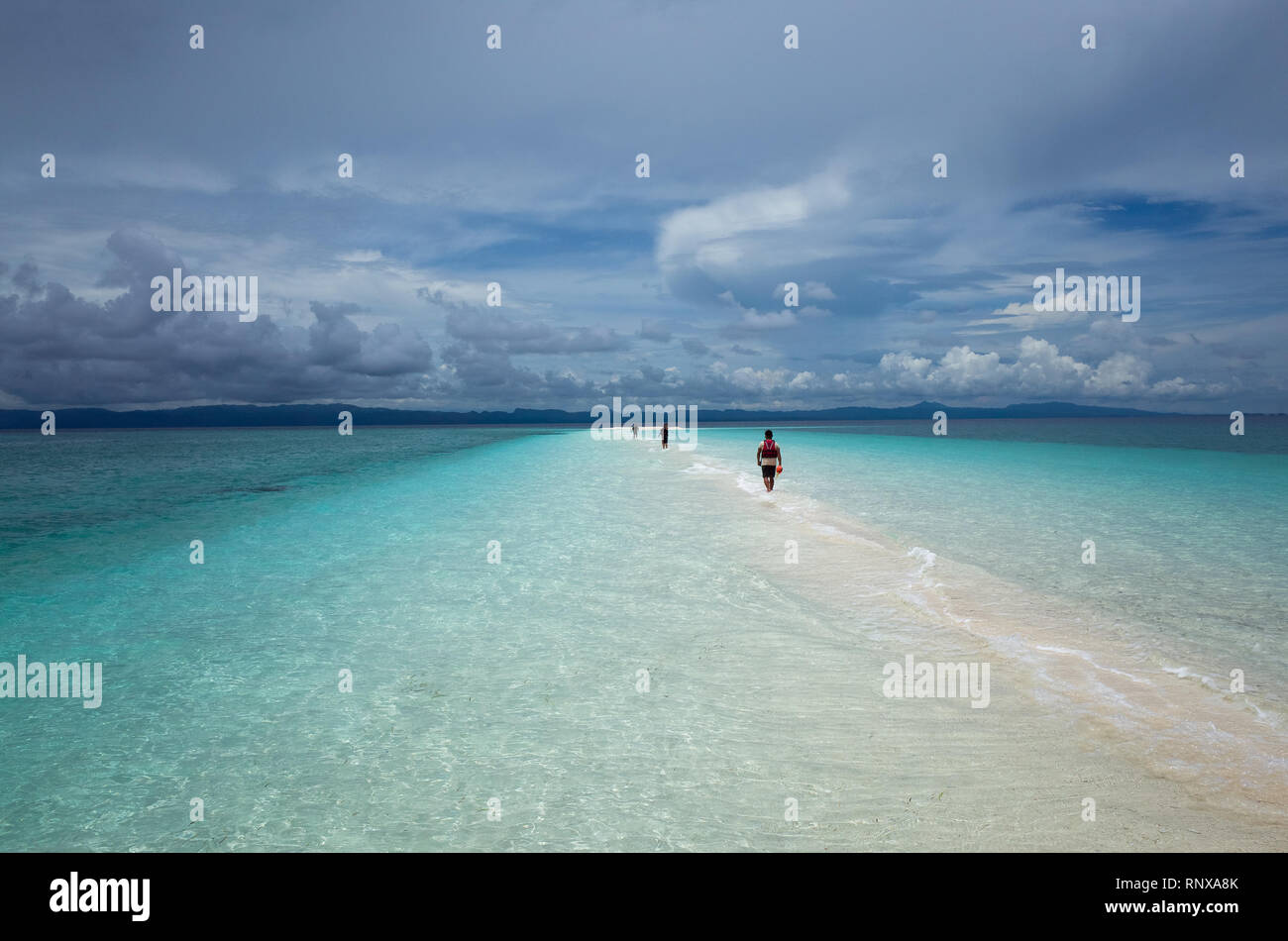 Filipino lifeguard walking after tourists on white sandbar at high tide ...