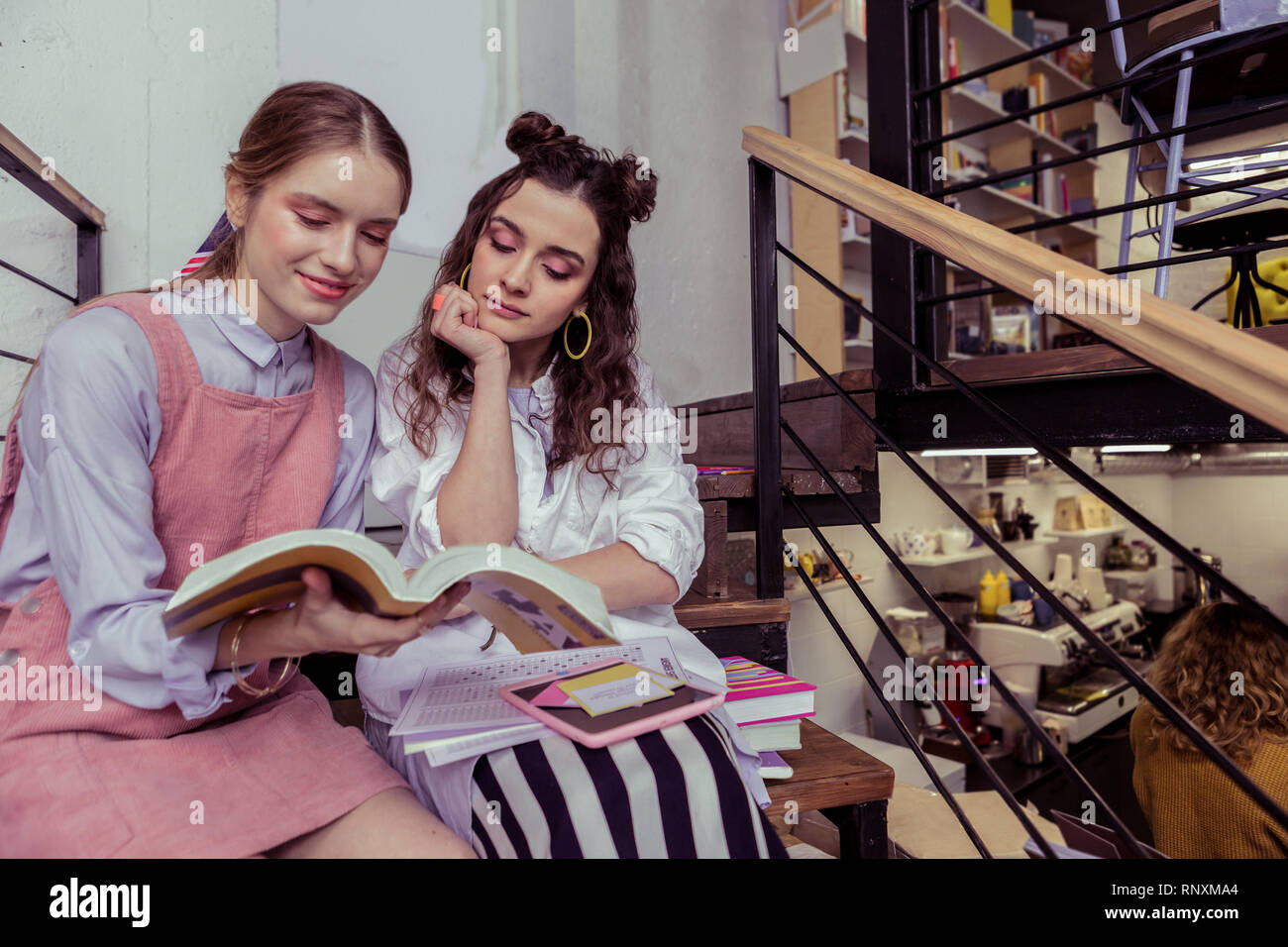 Calm and peaceful girls sitting shoulder to shoulder and reading book ...