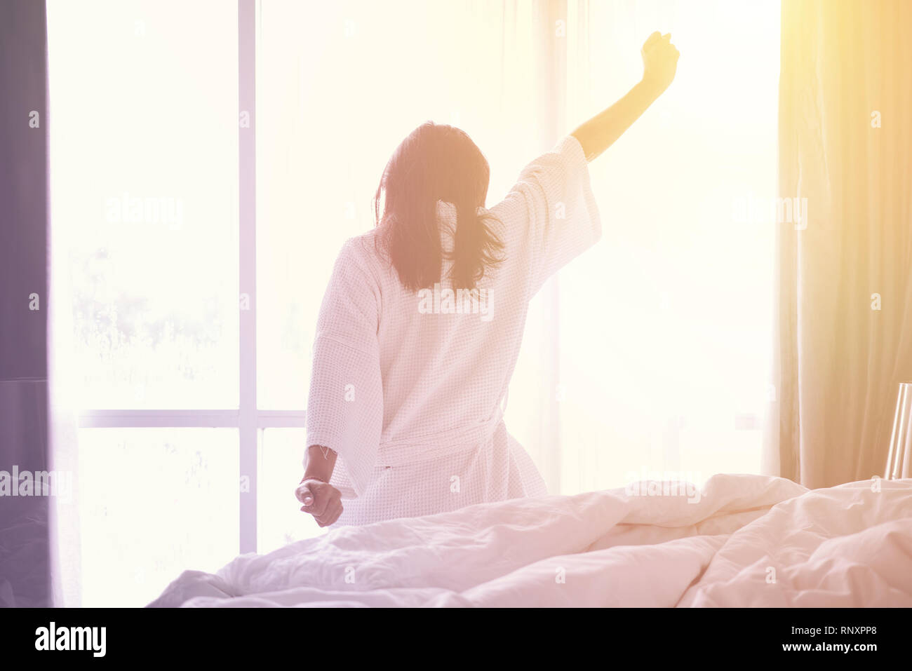 Woman stretching hands on bed after waking up while sitting on bed ...