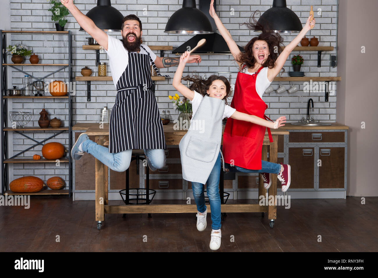 Having fun in kitchen. Family mom dad and little daughter wear aprons ...
