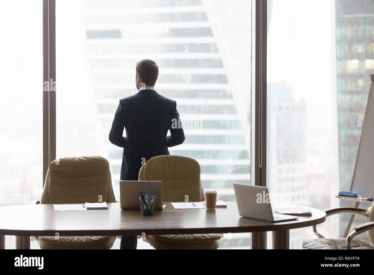 Rear view at successful businessman standing back in modern office ...