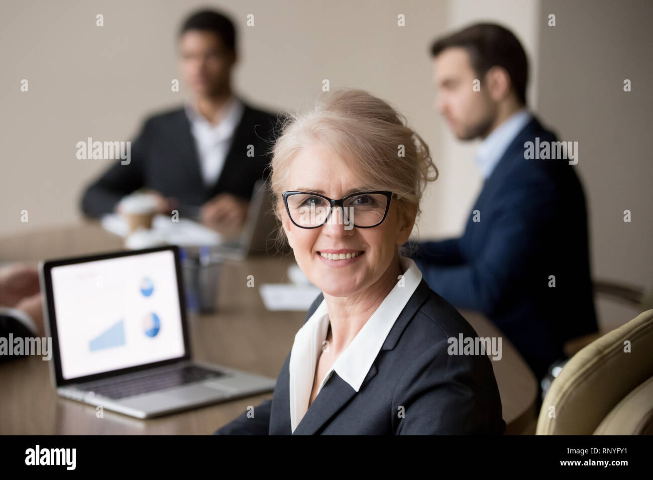 Happy middle-aged businesswoman in glasses posing at team office ...