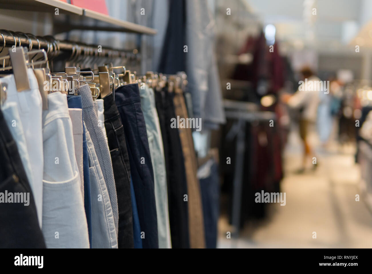 Row of pants and jeans on the racks in clothing store, shopping. Blur ...