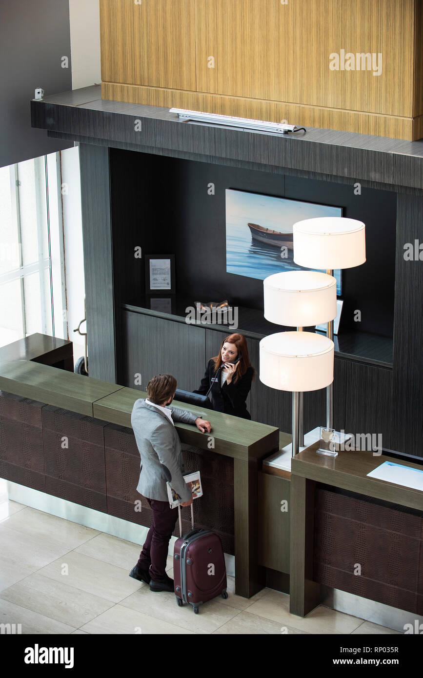 Female receptionist talking on telephone while businessman standing at ...