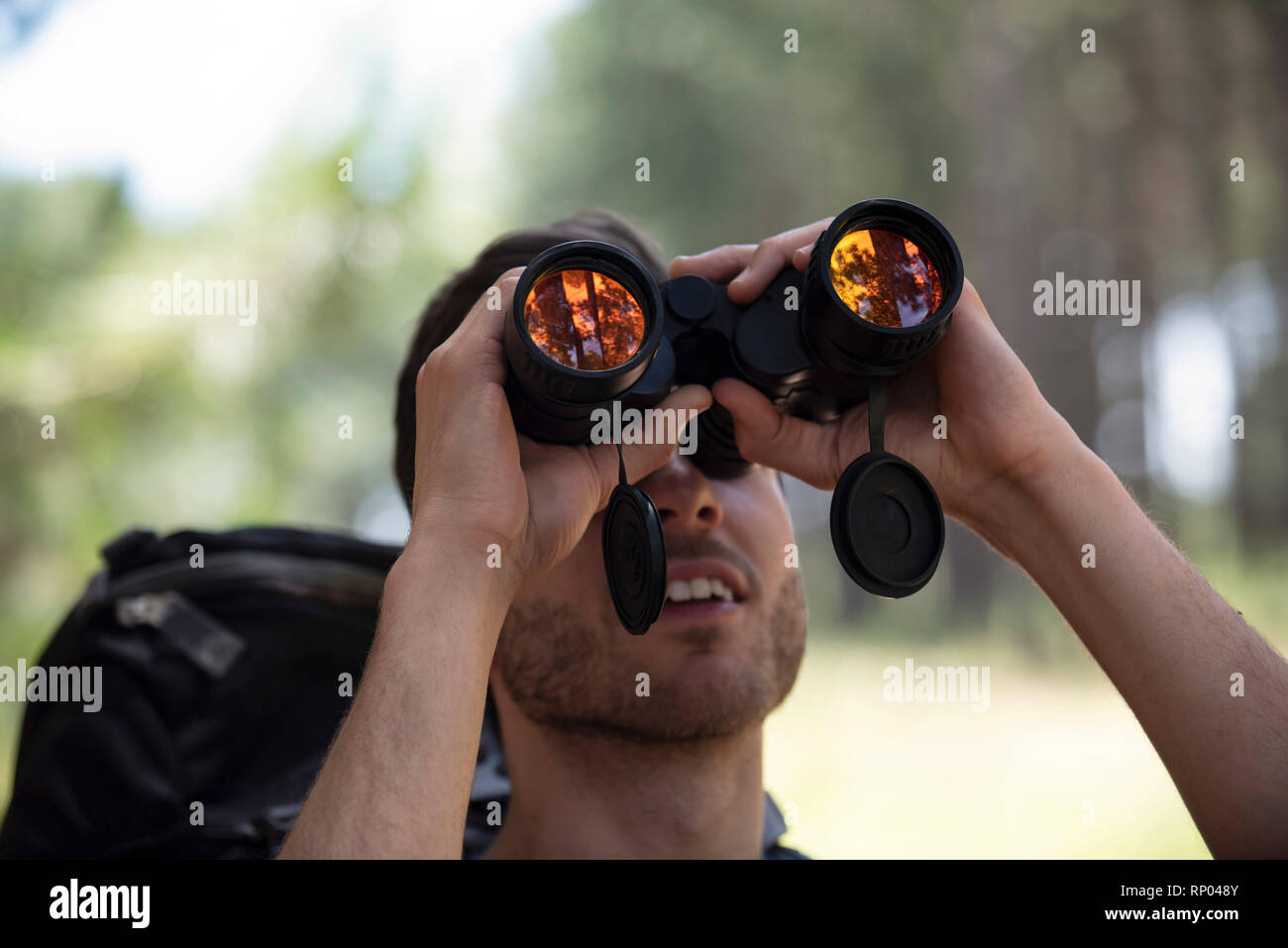 Young man looking through binoculars in forest Stock Photo - Alamy