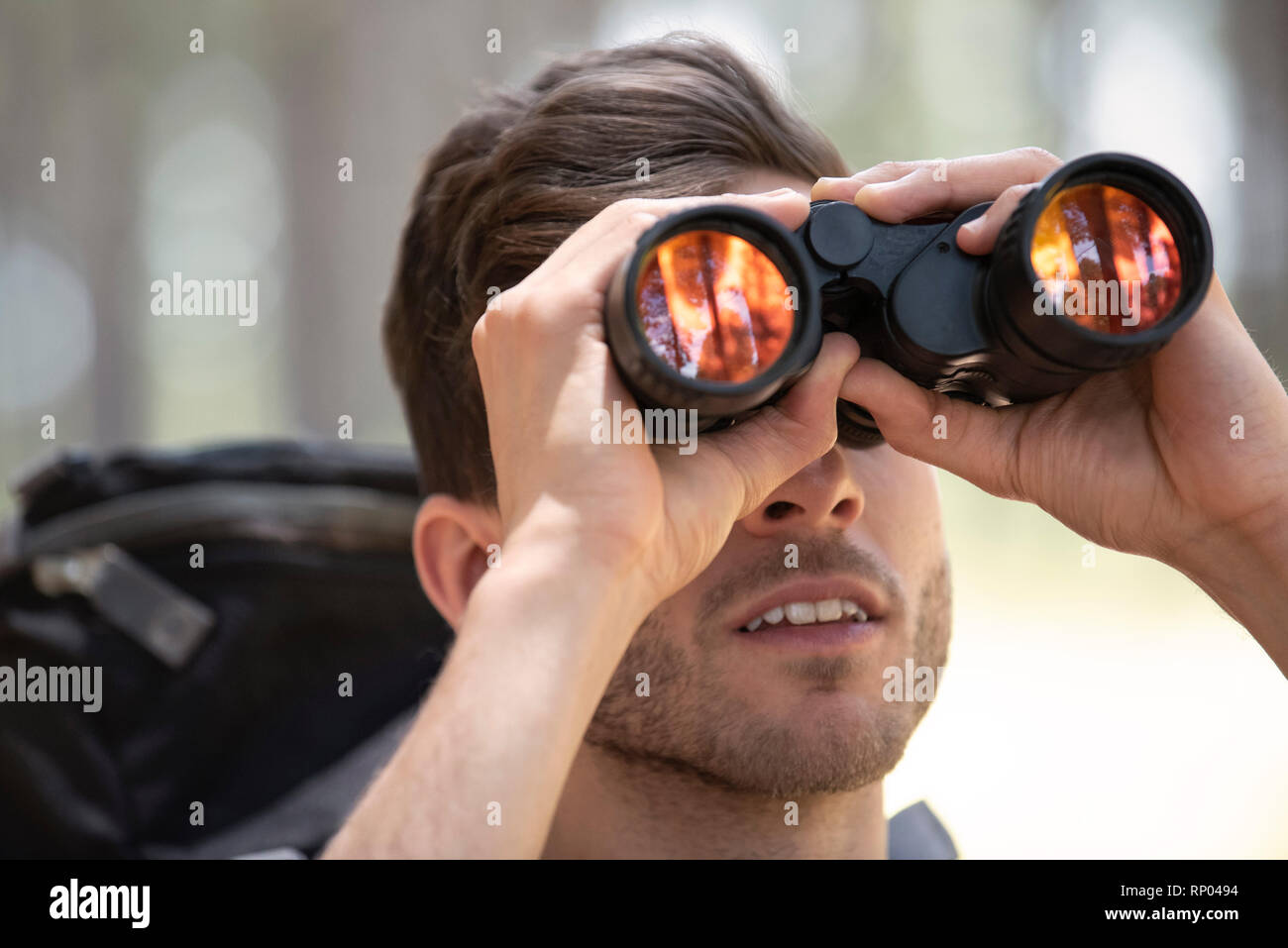Young man looking through binoculars in forest Stock Photo - Alamy