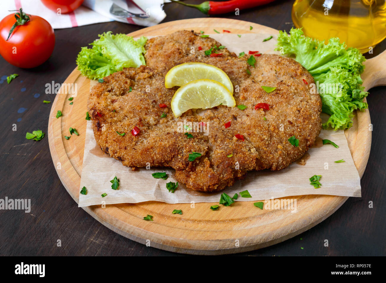 Large Viennese schnitzel on a wooden board with lemon on a dark ...