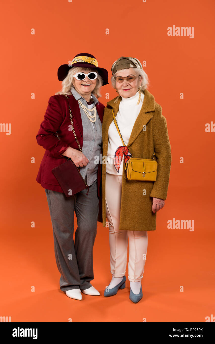 stylish retired women standing and smiling on orange background Stock ...