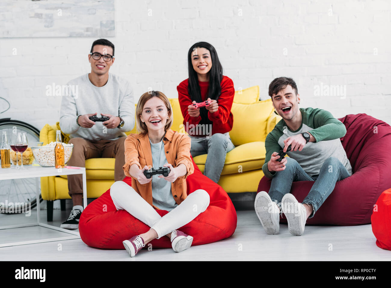 excited multicultural friends playing video game and enjoying snacks ...