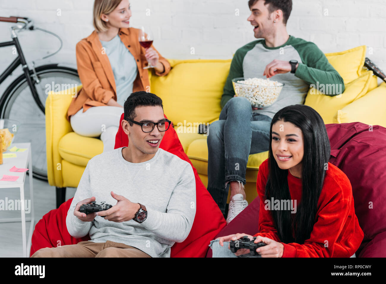 cheerful multicultural friends playing video game and enjoying drinks ...