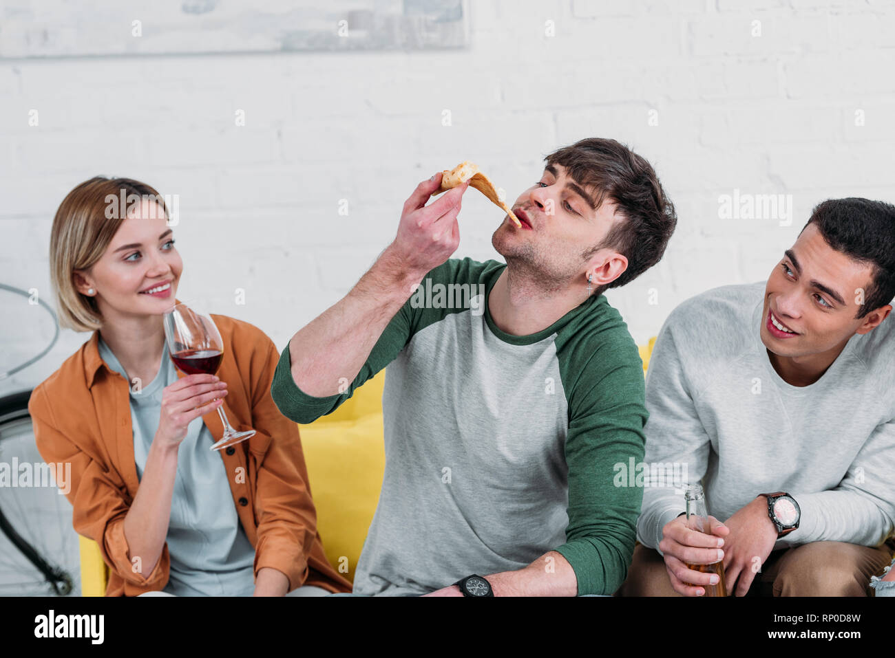 handsome young man eating pizza sitting while multicultural friends ...