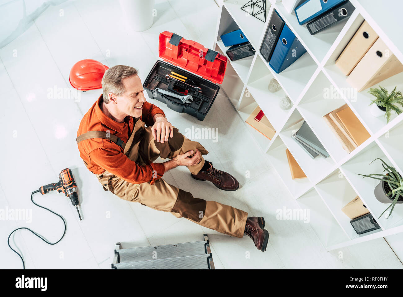 top view of repairman sitting on floor with injured knee in office ...